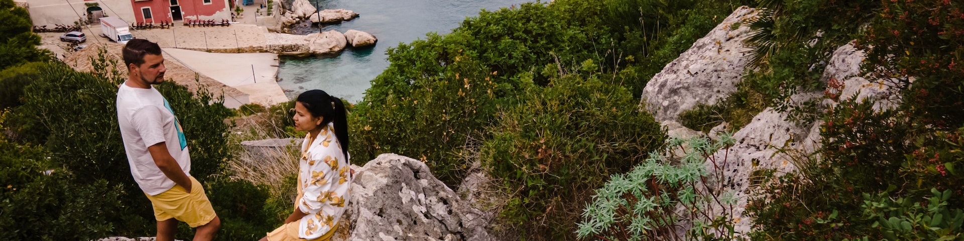 Paisagem costeira com afloramentos rochosos, mar azul cristalino e um pequeno edifício de fachada vermelha.