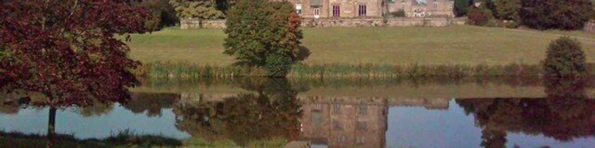 Uma grande propriedade com lago, árvores e um edifício semelhante a um castelo ao fundo.