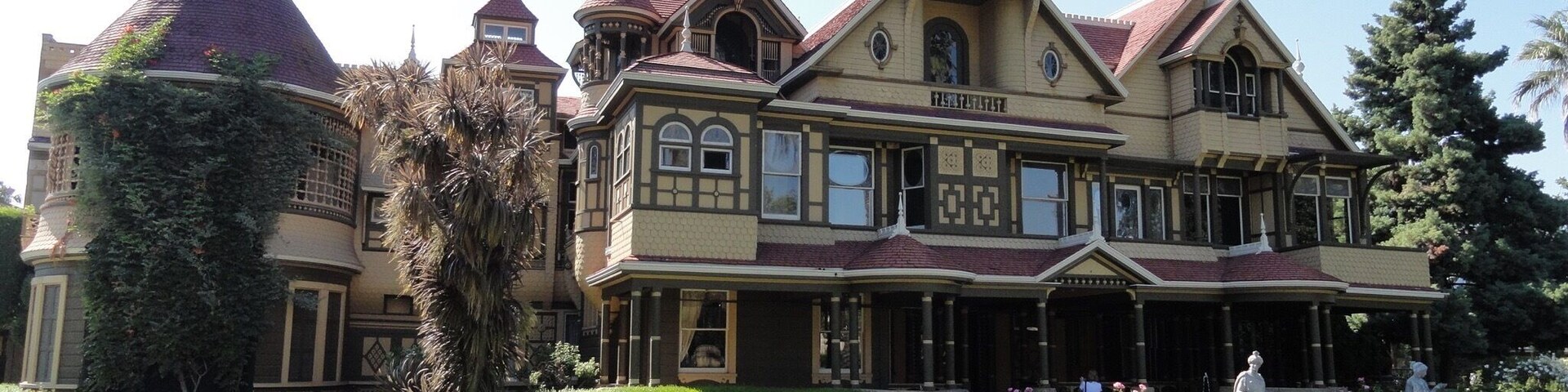 Uma grande e elaborada mansão em estilo vitoriano, com várias torres e um jardim bem cuidado.