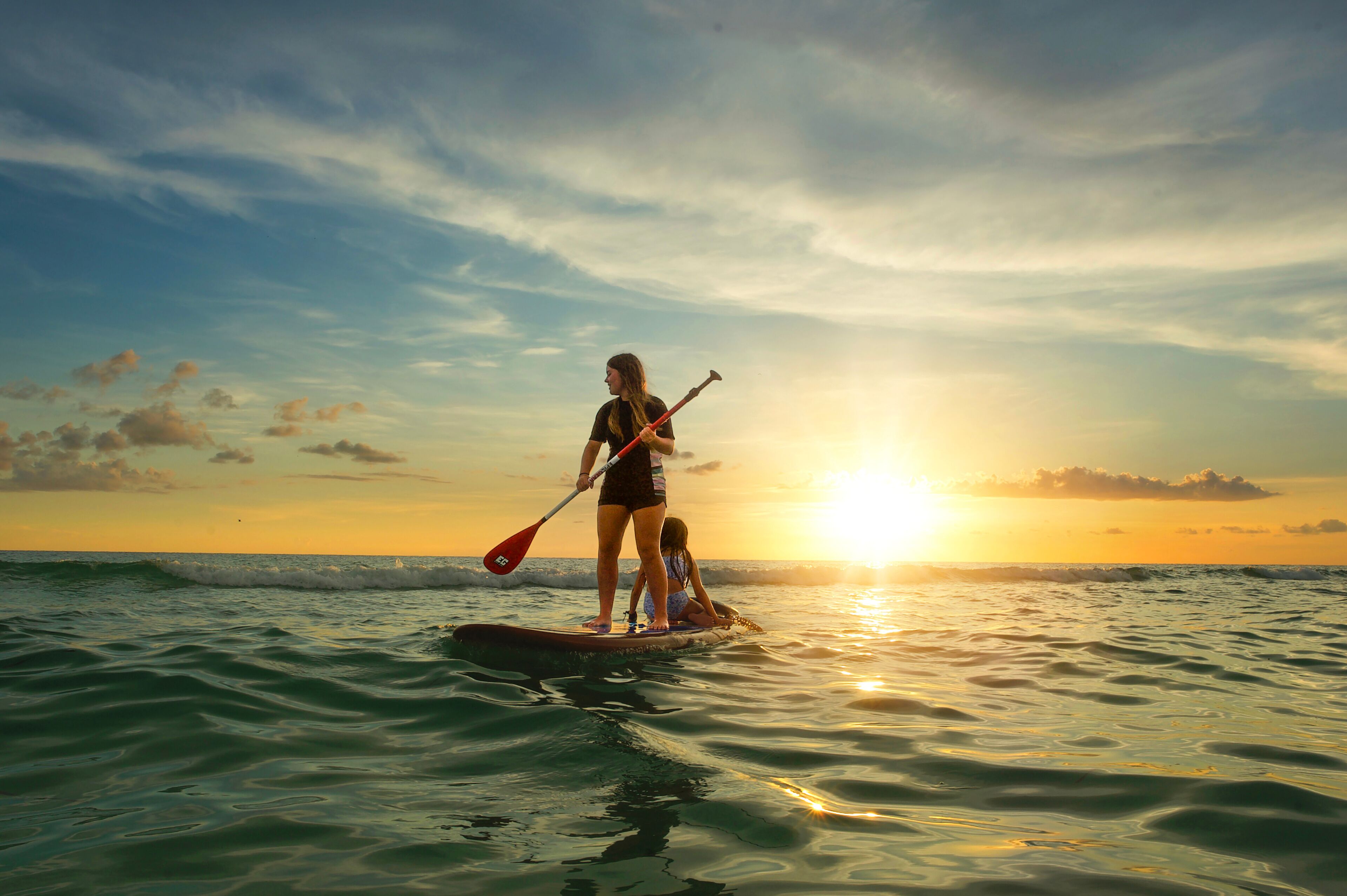 Alguém praticando paddleboarding em um mar calmo durante o pôr do sol.