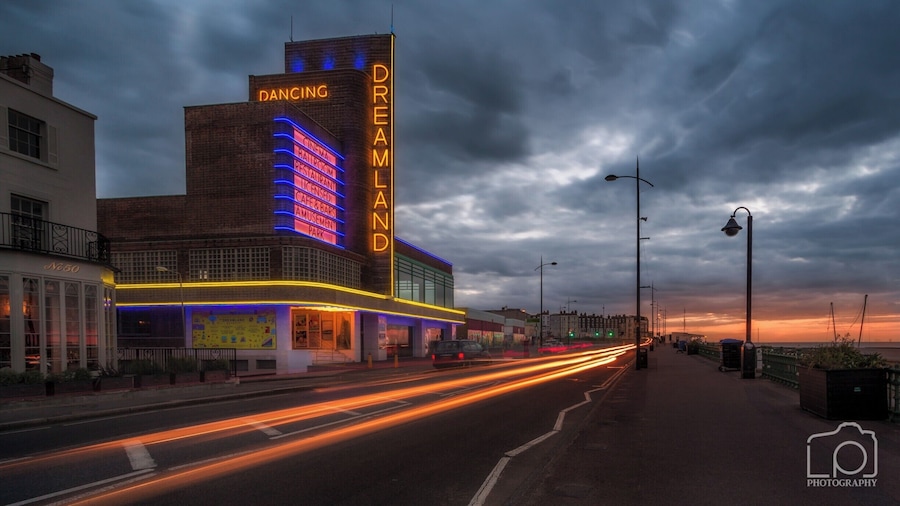 Um edifício iluminado com neon e placas indicando cinema, restaurante e parque de diversões.