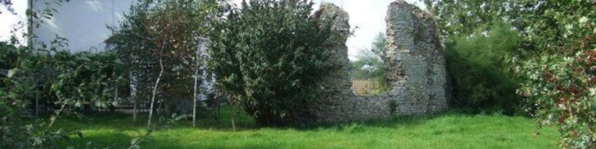 Uma casa branca, ruínas de pedra e vegetação exuberante.