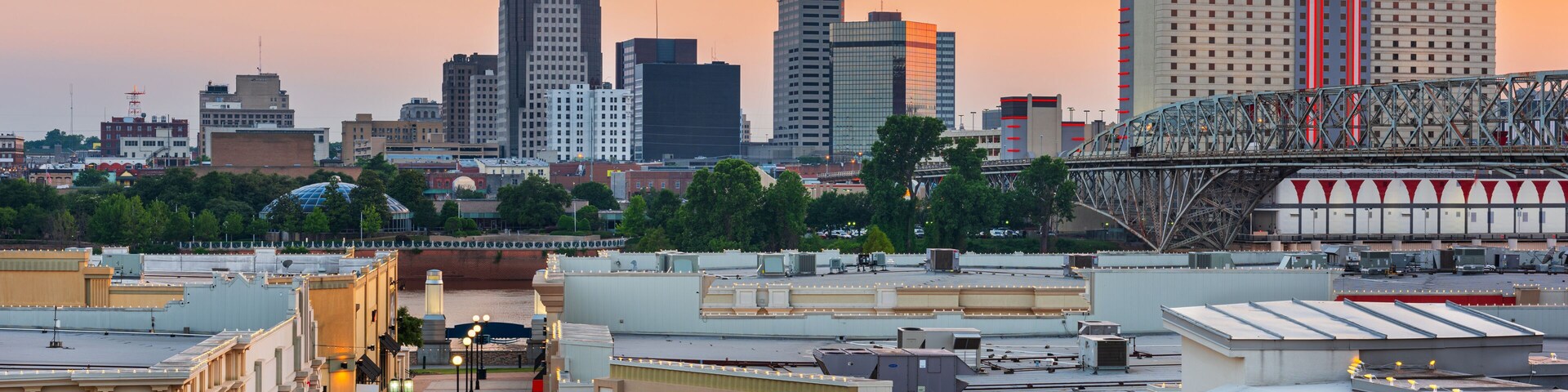 Paisagem urbana ao pôr do sol, com edifícios modernos e uma ponte histórica.