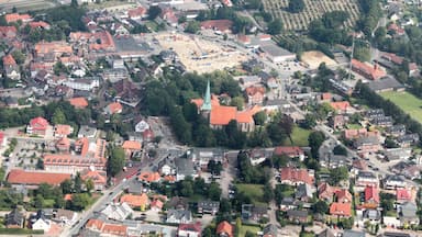 Vista aérea de uma cidade com edifícios de telhados vermelhos, uma igreja e um grande campo aberto.