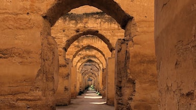 Um corredor comprido com arcos e chão de terra.