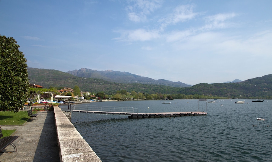 Um lago tranquilo com barcos, um cais e montanhas ao fundo.