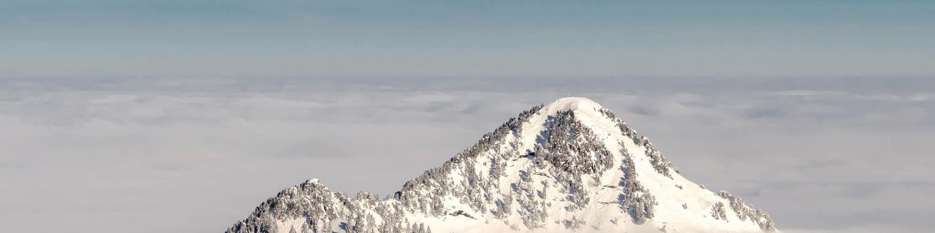 Pico de montanha coberto de neve, rodeado por nuvens.