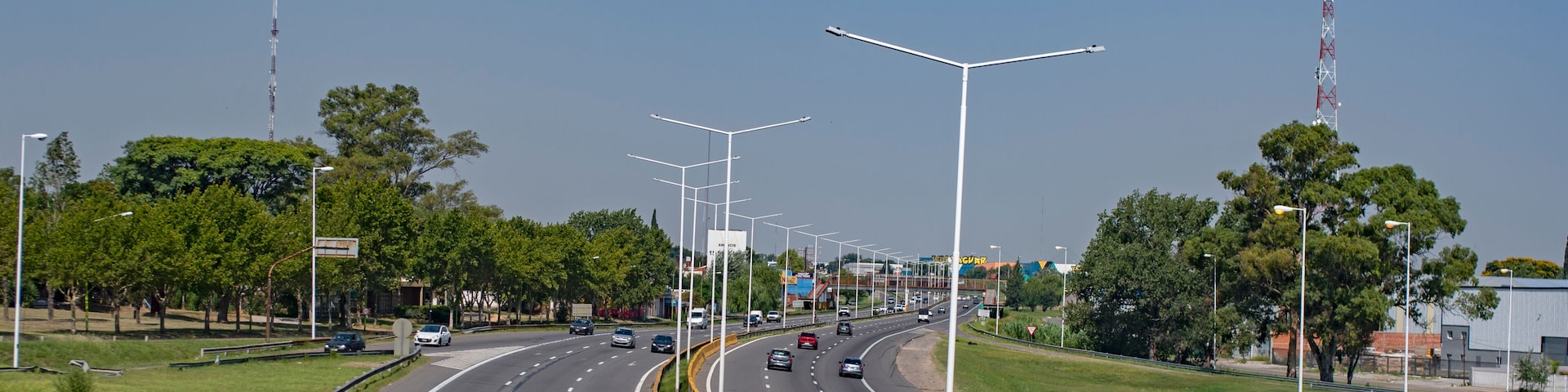 Uma autoestrada com múltiplas faixas, iluminação pública, uma curva e vegetação nas laterais.