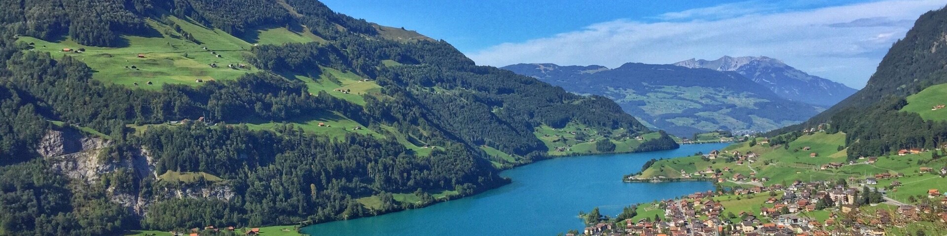 Paisagem montanhosa com um rio, uma cidadezinha e campos verdes.