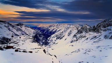 Cordilheira coberta de neve, céu claro e um teleférico no vale.