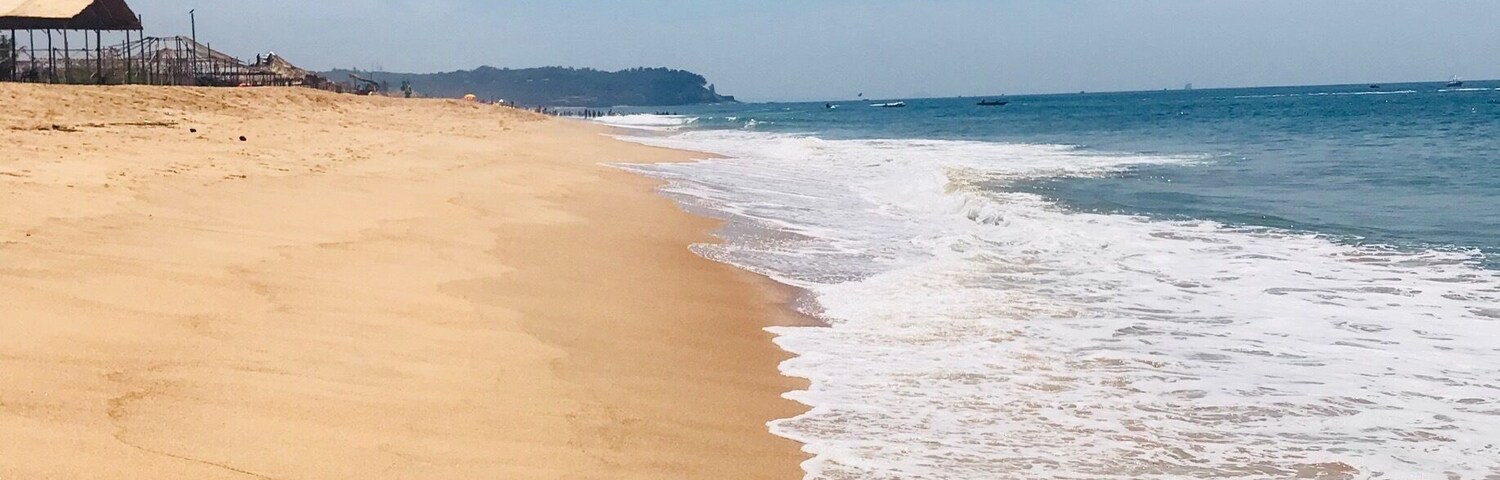 Praia arenosa com ondas suaves e céu claro.
