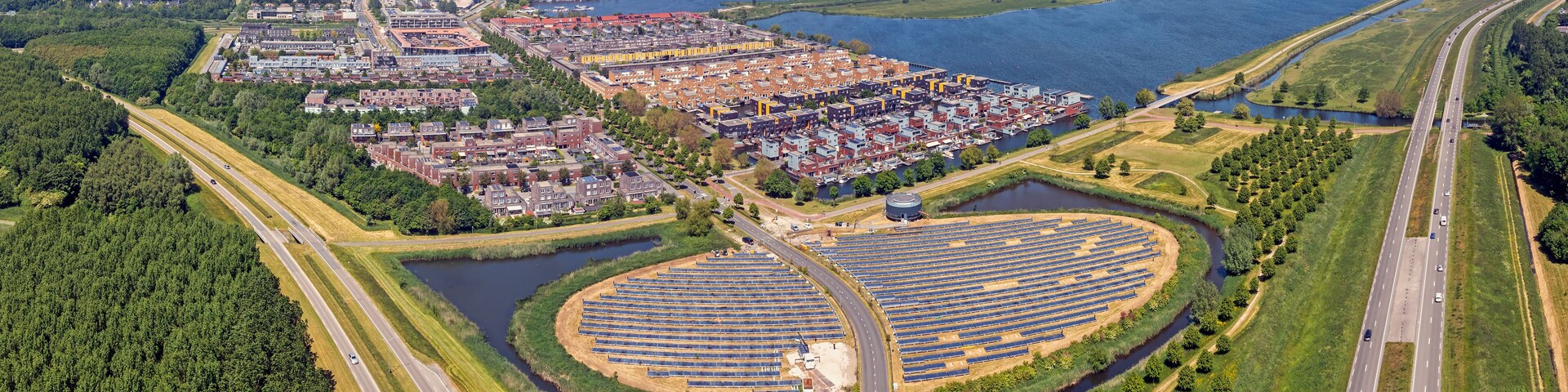 Vista aérea de uma cidade costeira com uma grande marina, uma autoestrada e um parque solar.