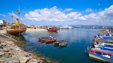 Um porto com barcos atracados na costa, uma praia de areia e um céu azul e límpido.