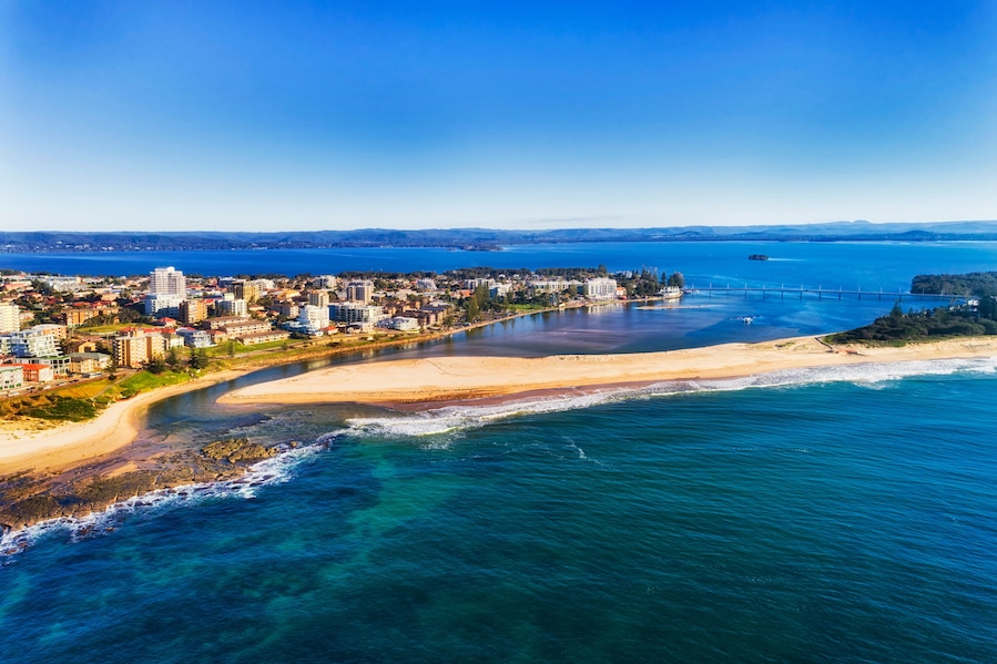 Uma cidade costeira com uma praia, uma ponte e uma grande extensão de água.
