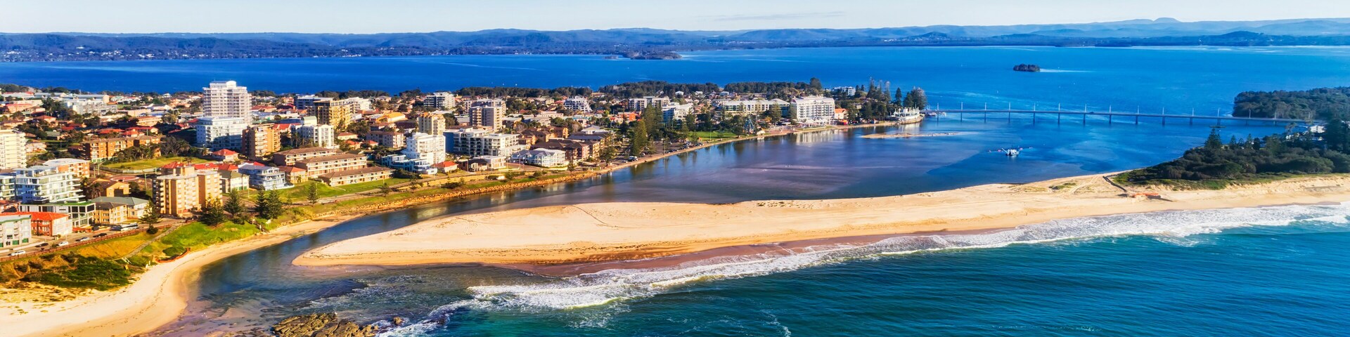 Uma cidade costeira com uma praia, uma ponte e uma grande extensão de água.