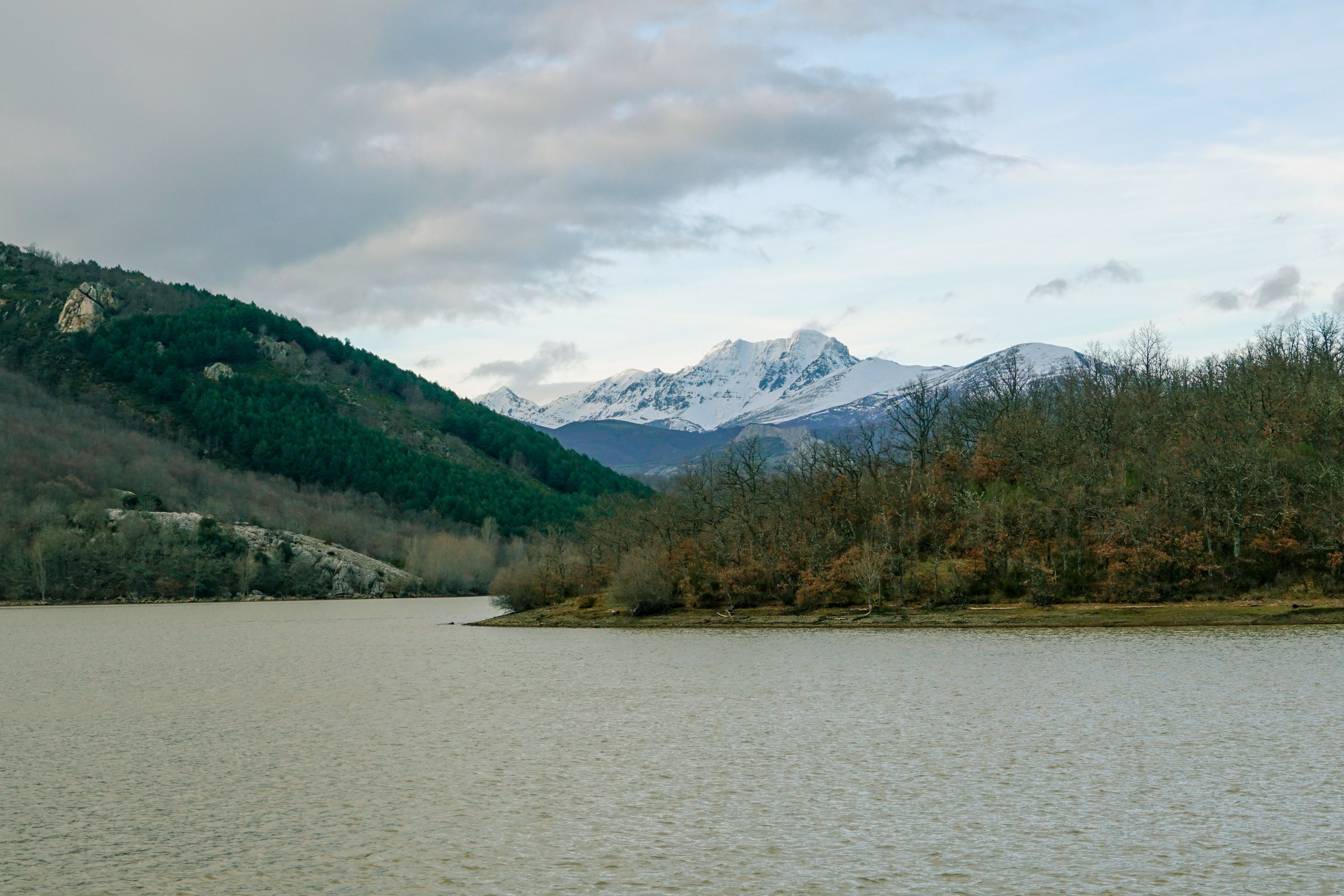 Um lago tranquilo rodeado por colinas arborizadas e uma cordilheira nevada ao longe.