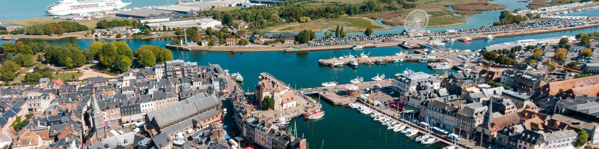 Uma cidade costeira com edifícios históricos, um porto de iates e uma grande ponte ao longe.