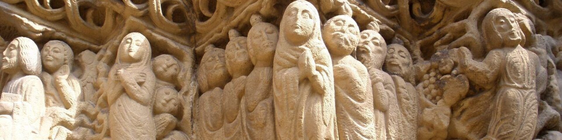 Escultura em pedra detalhada com figuras vestidas em túnicas, padrões intrincados e uma figura central segurando uma criança.
