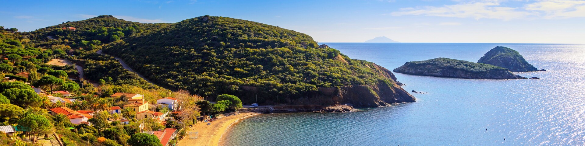 Paisagem costeira com uma praia arenosa, colinas verdejantes e um mar azul cristalino.