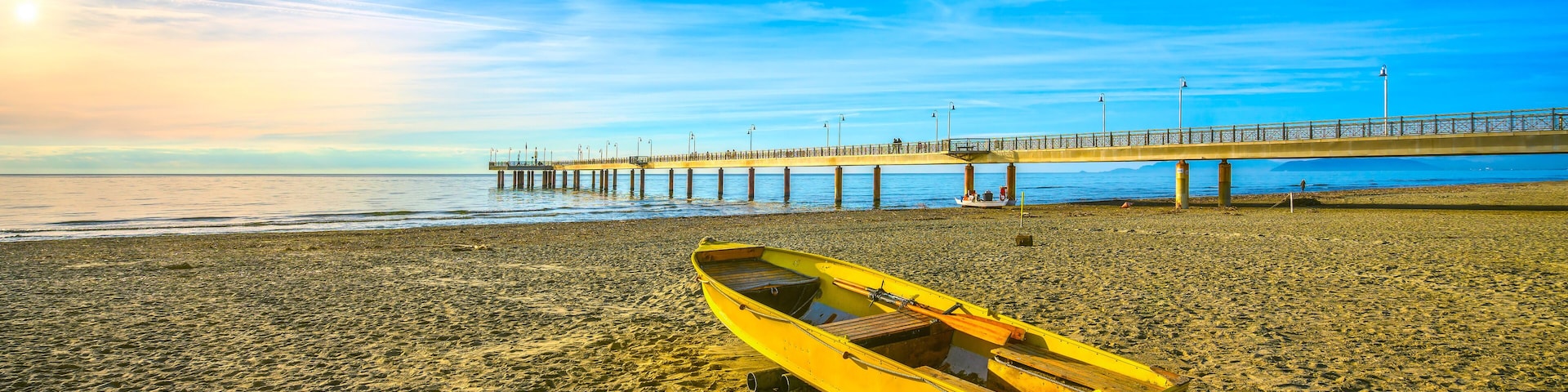 Uma praia arenosa com um barco amarelo e um cais que se estende até a água.