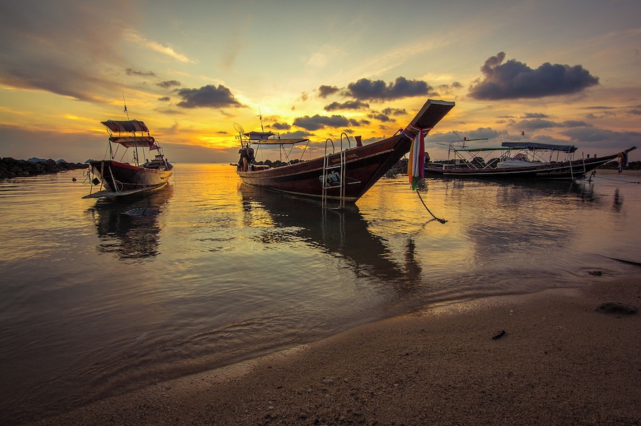 Três barcos tradicionais ancorados em águas calmas durante o pôr do sol.