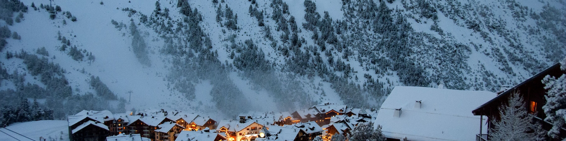 Vila montanhosa coberta de neve, com edifícios de madeira e pista de esqui.