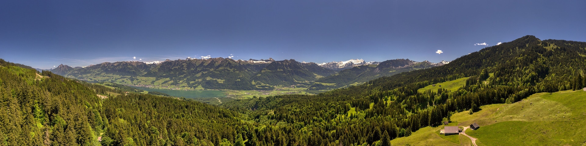 Paisagem montanhosa com florestas densas, um lago e um pequeno edifício.