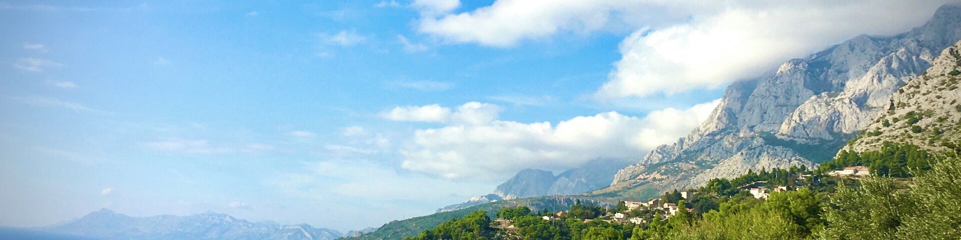Paisagem montanhosa com céu claro, um caminho de terra e uma cidade no vale.