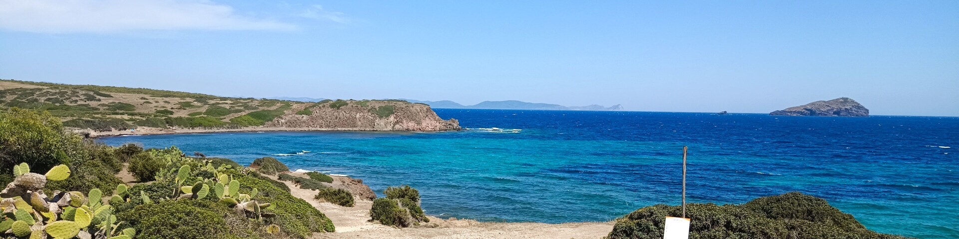 Paisagem costeira com mar azul claro, falésias rochosas e vegetação rasteira.