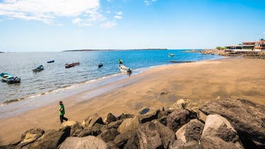 Uma praia com barcos, pedras e um céu claro.