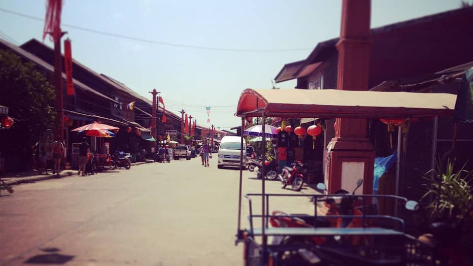 Rua com lojas, motos e uma van branca.