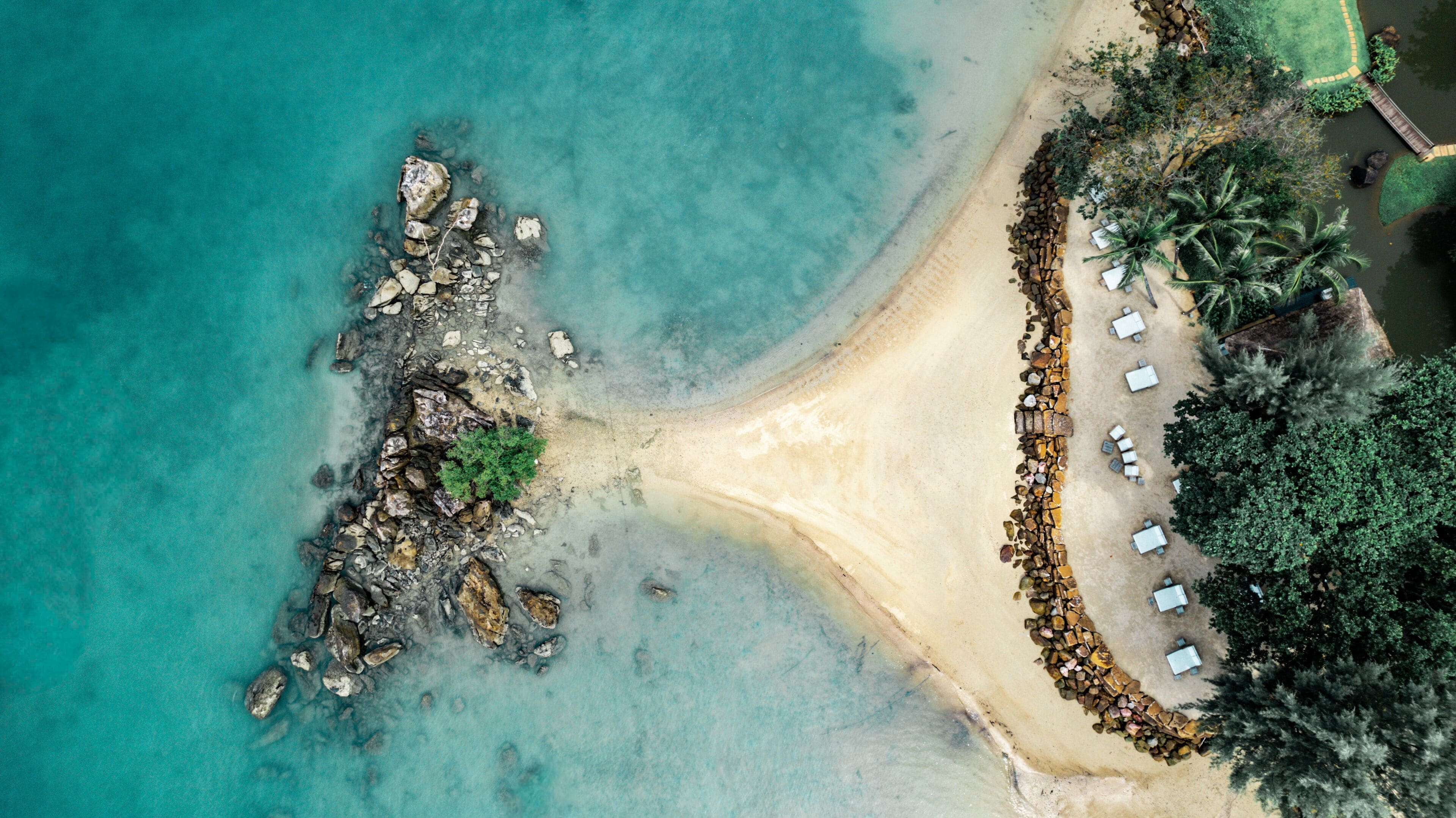 Uma praia com águas turquesa cristalinas, um afloramento rochoso e uma fileira de cadeiras de praia brancas.
