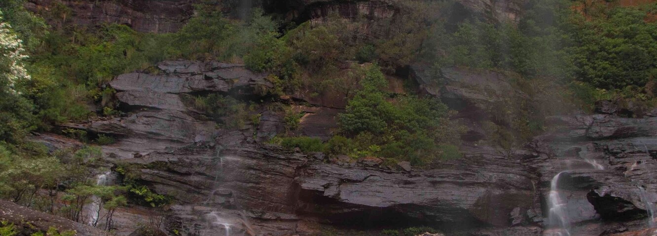 Uma cascata desce por um penhasco rochoso, com vegetação exuberante na base.