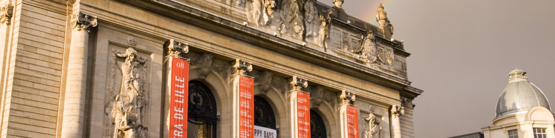 Uma casa de ópera histórica com esculturas elaboradas e um arco-íris no céu.