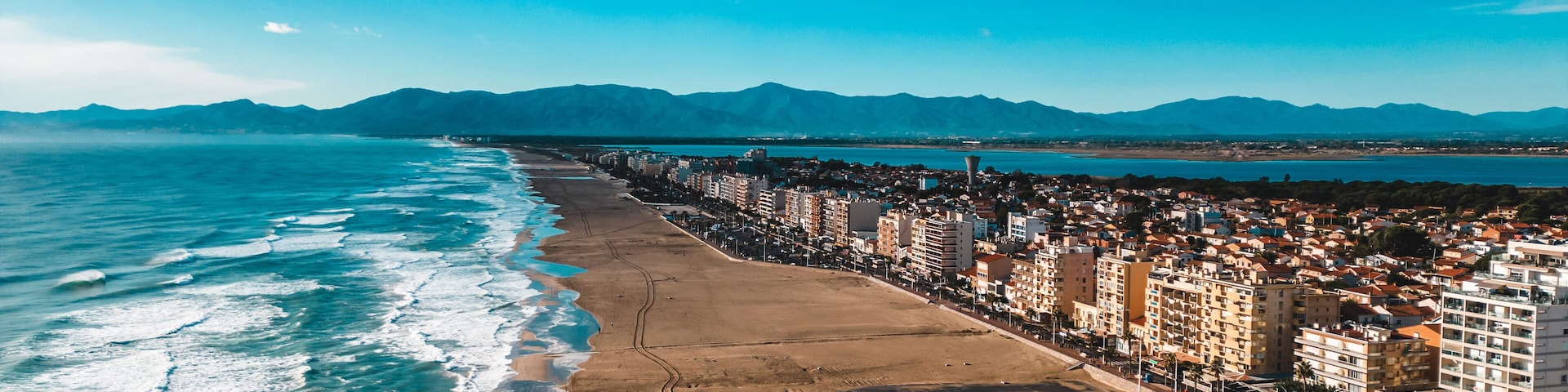 Uma cidade costeira com praia, edifícios e montanhas ao fundo.