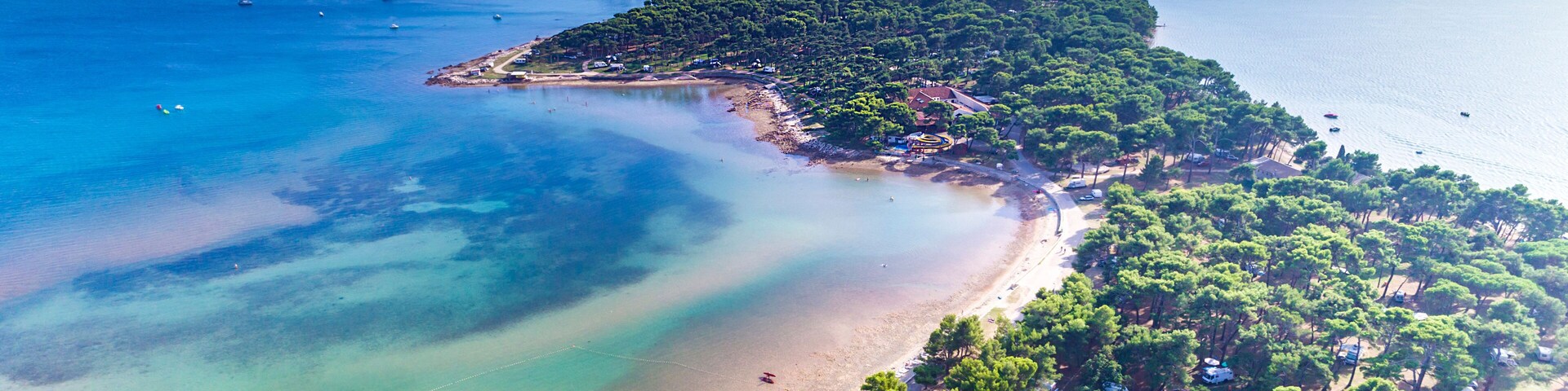 Vista aérea de uma área costeira com praia, águas cristalinas e uma ilha densamente arborizada.