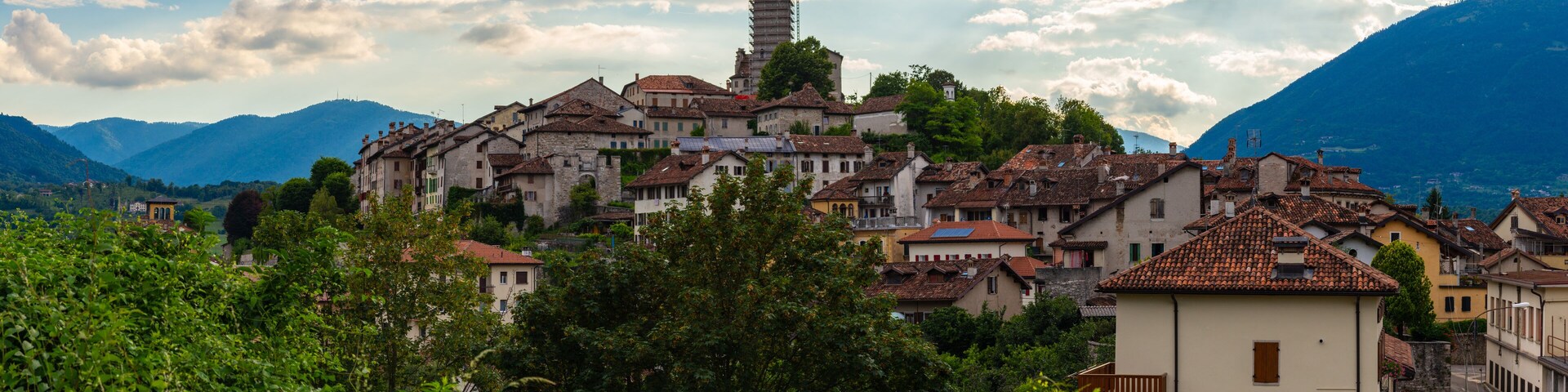 Uma cidade montanhosa com edifícios de telhado em terracota, vegetação exuberante e uma torre imponente.
