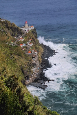 Uma vila costeira com um farol, casas e falésias rochosas.