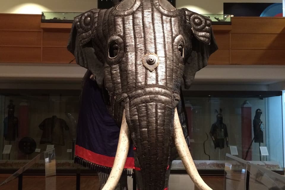 Uma grande estátua de elefante com um cavaleiro, rodeada por exposições de museu.