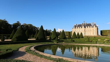 Um jardim formal com um lago espelhado, sebes bem aparadas e um grande edifício histórico.