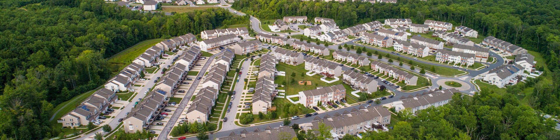 Uma área residencial com casas dispostas em formato circular, cercada por florestas densas e um lago.