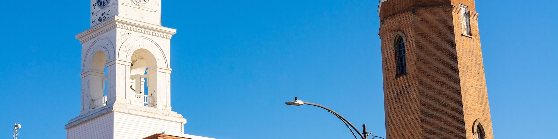 Uma torre do relógio branca com um relógio em cada lado e uma torre menor à direita.