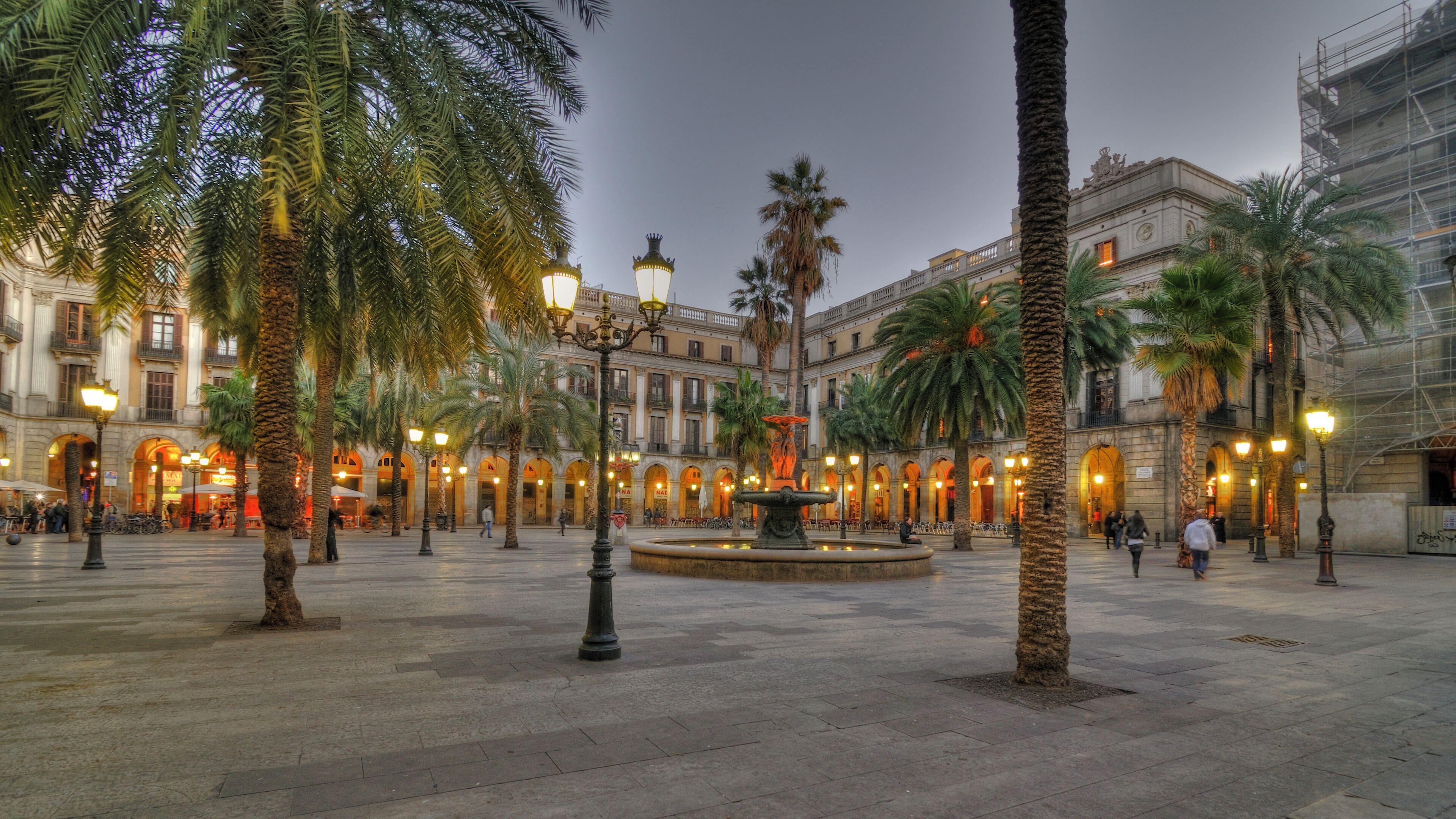 Uma praça com palmeiras, uma fonte e edifícios históricos.