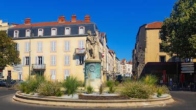 Uma rotatória com uma estátua, rodeada por edifícios com fachadas em tons pastel e telhados de telha vermelha.