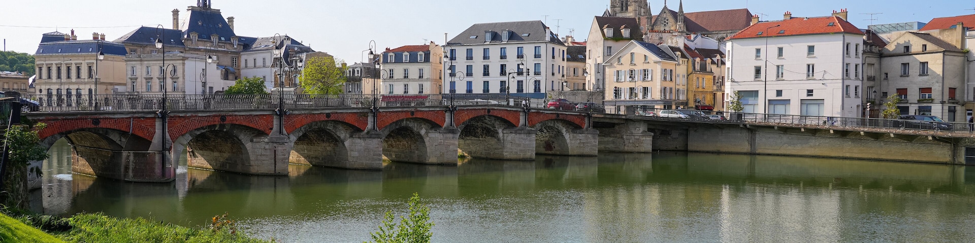 Uma ponte de pedra sobre um rio calmo, rodeada por edifícios históricos e uma torre de igreja imponente.