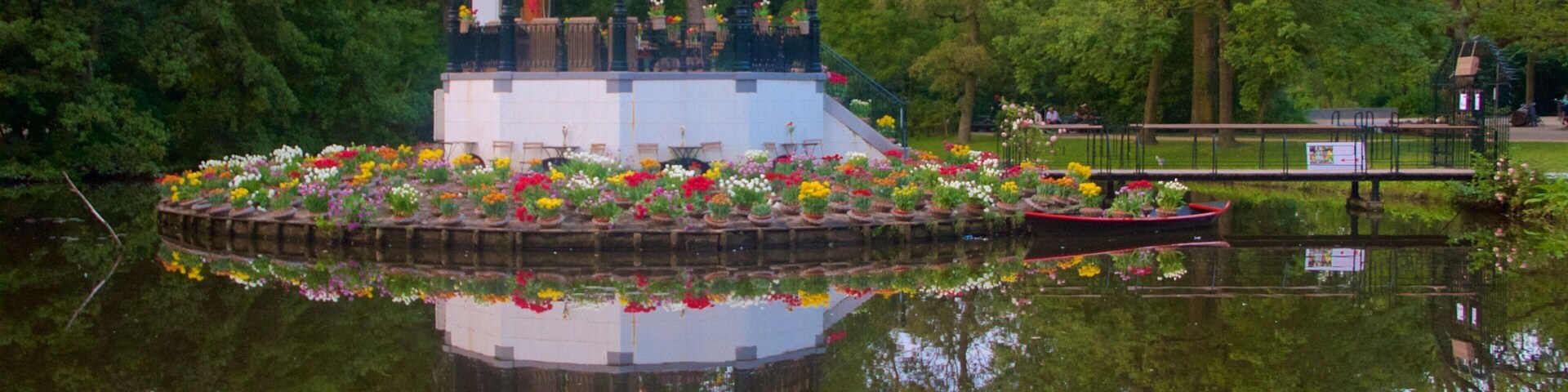 Um gazebo com um jardim de flores no centro de um lago, cercado por árvores.