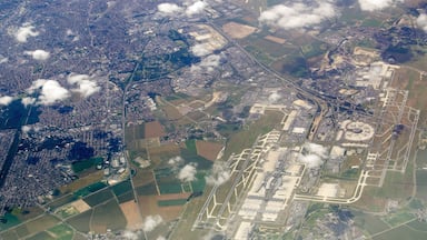 Vista aérea de uma cidade com um aeroporto grande, campos ao redor e nuvens dispersas.