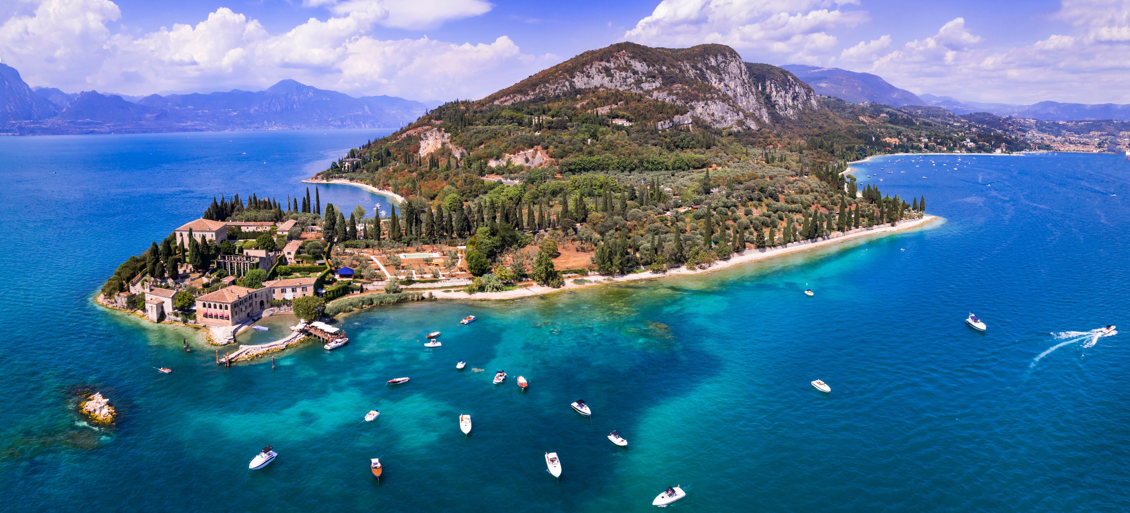 Uma vila costeira com montanha, mar azul cristalino e barcos.