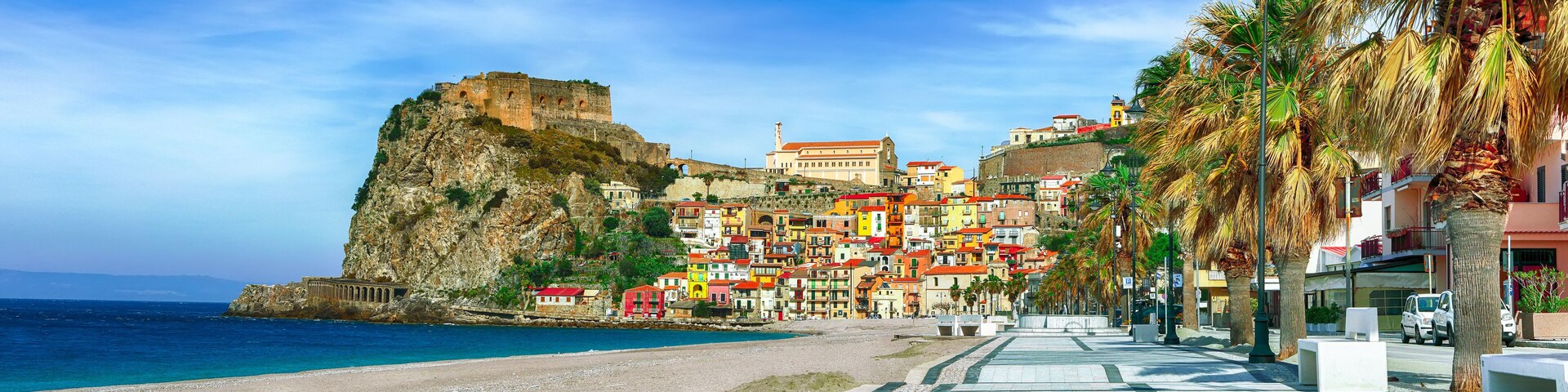 Uma vila costeira com edifícios coloridos, um rochedo imponente e uma praia.