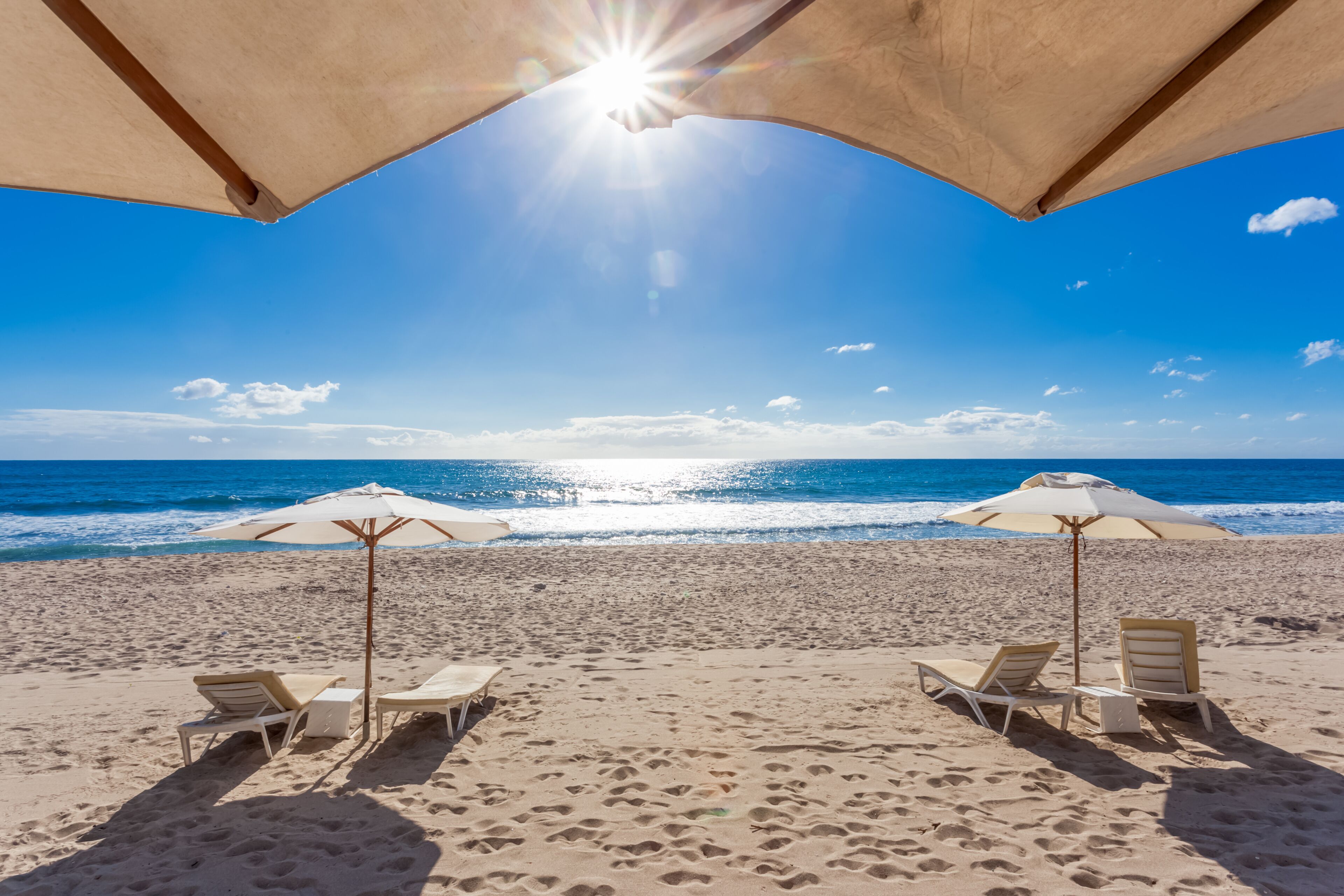 Uma praia com dois guarda-sóis e espreguiçadeiras voltadas para o oceano.